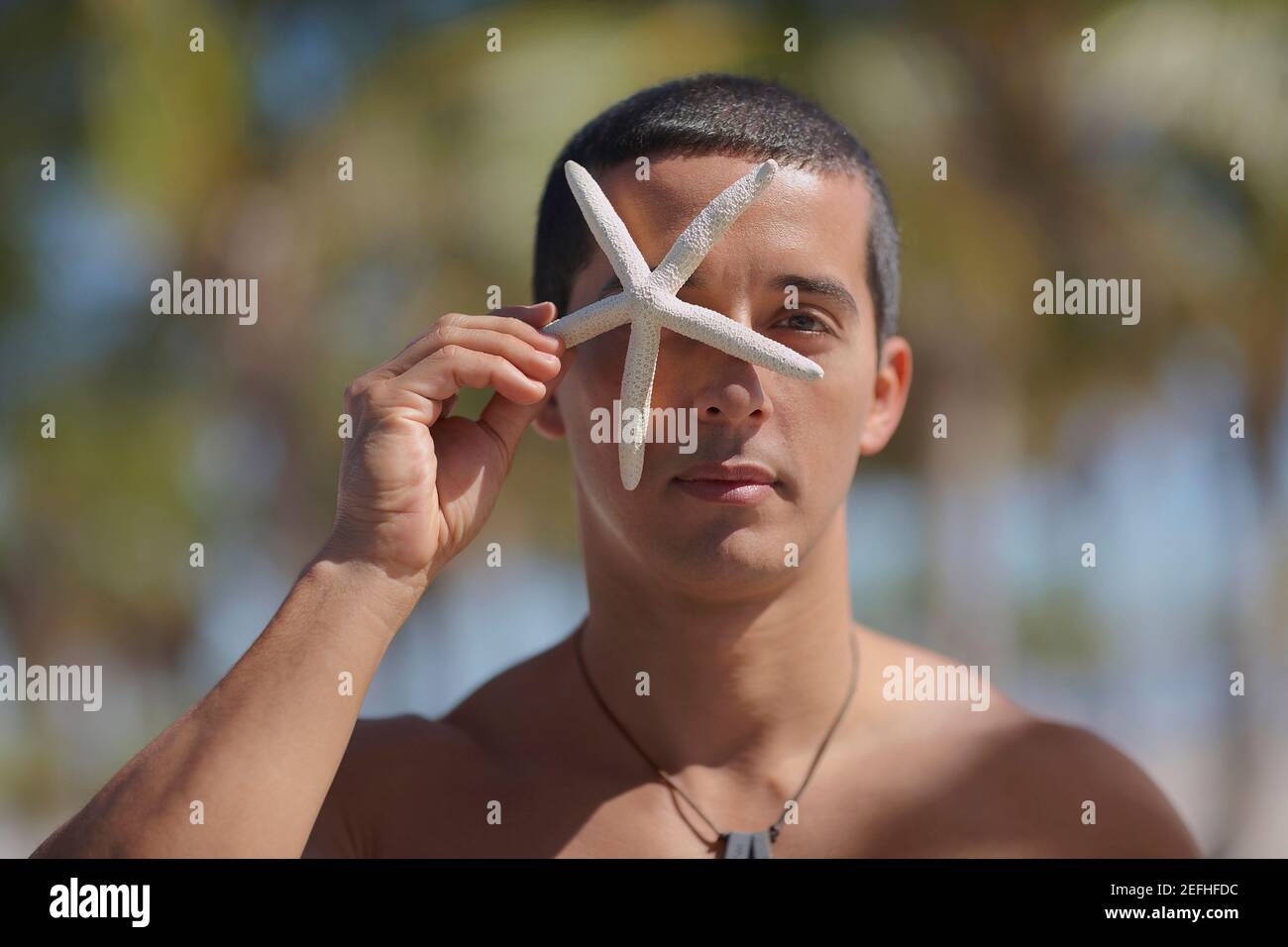 Portrait of a mid adult man holding a starfish in front of his face ...