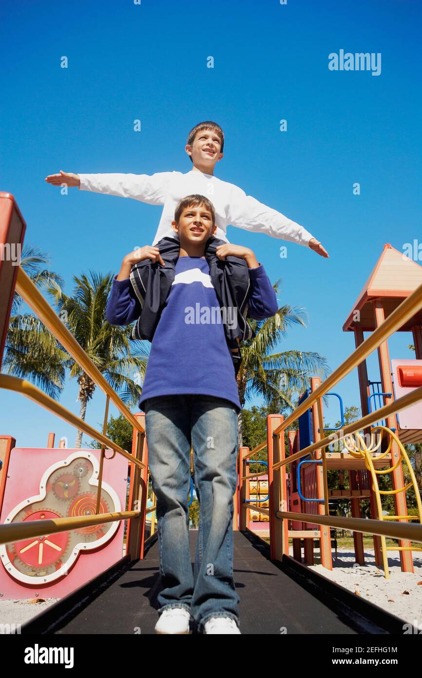 Low angle view of a teenage boy carrying his brother on his shoulder ...