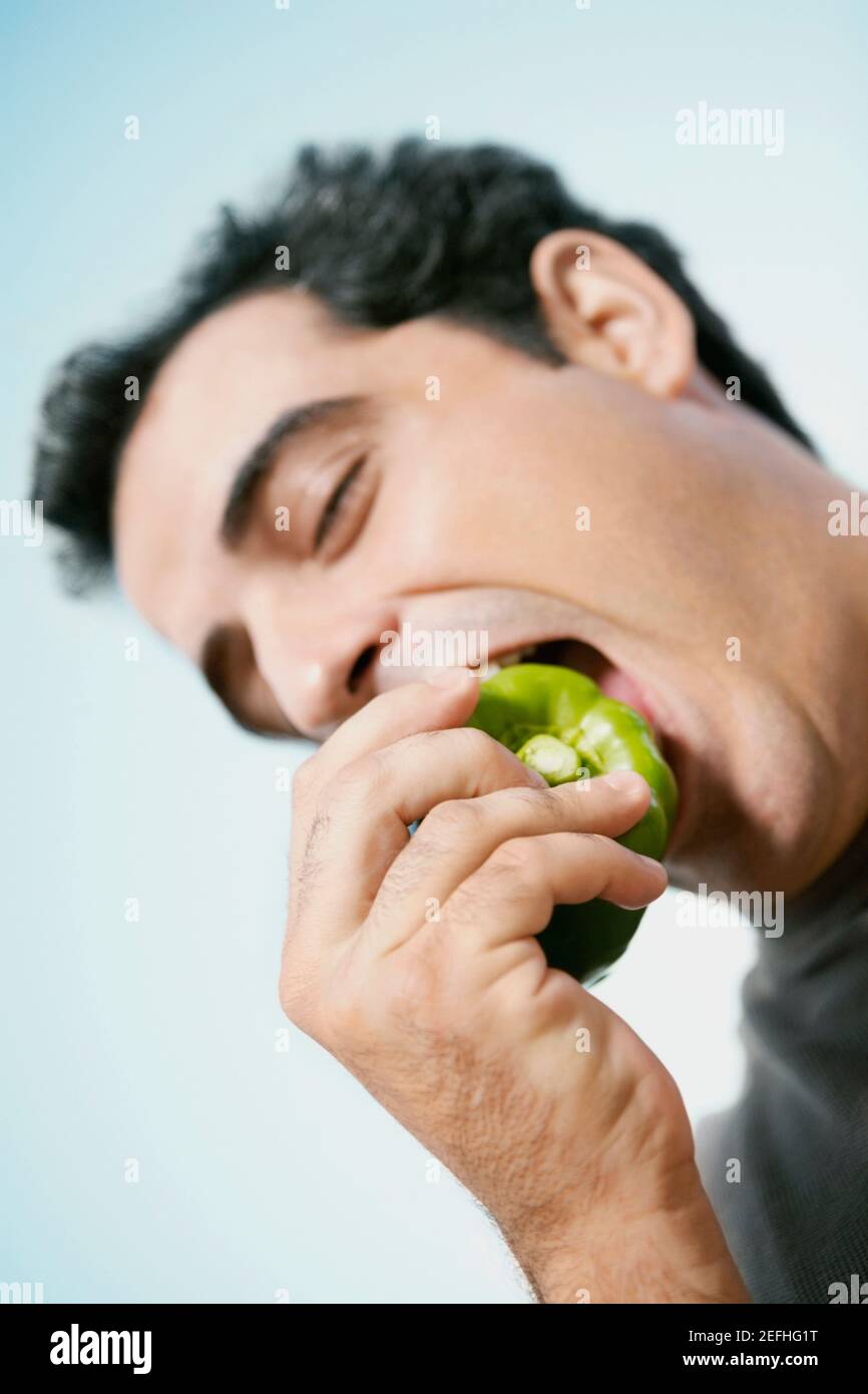 Mid adult man eating a green bell pepper Stock Photo - Alamy