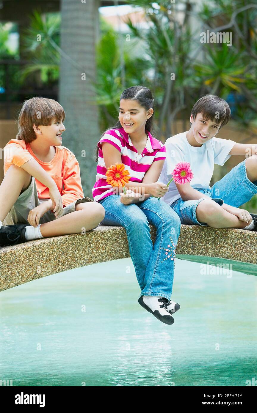 Girl sitting between two boys on a footbridge across a pond Stock Photo ...
