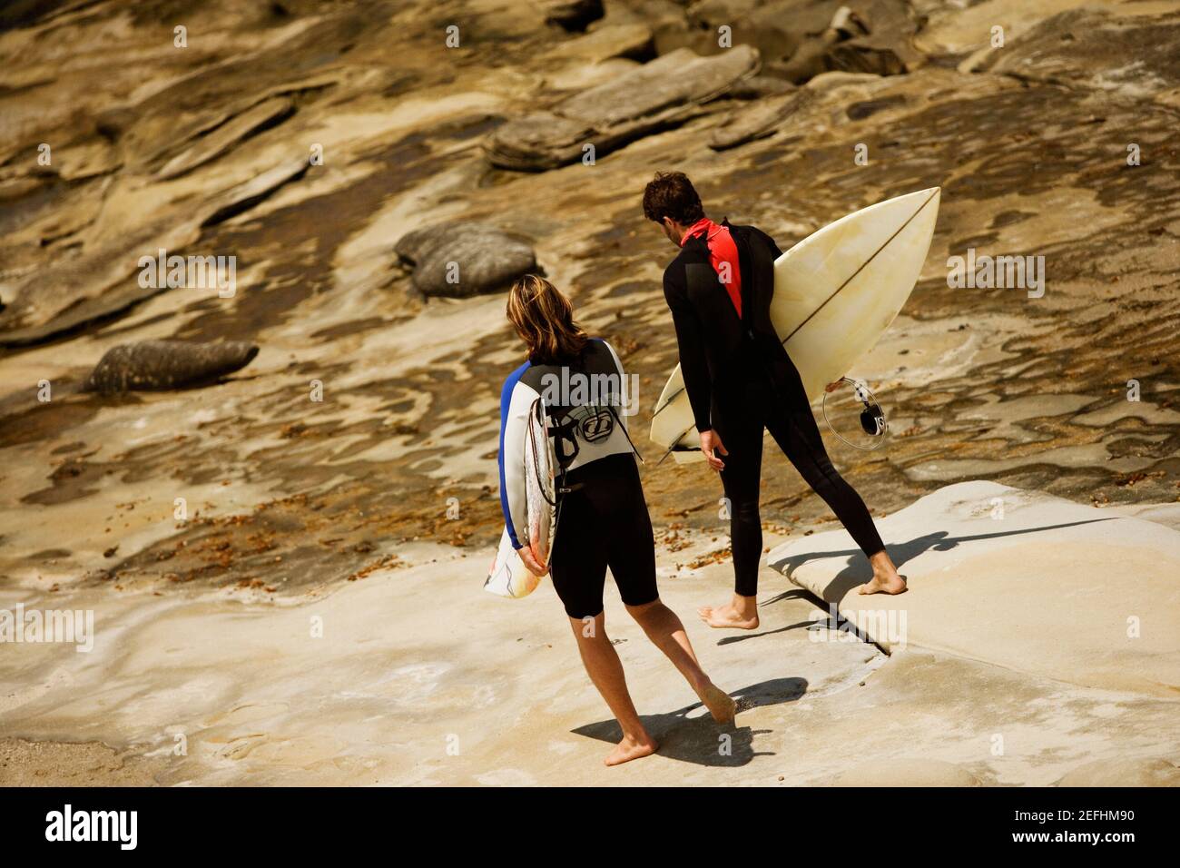 Rear view of two surfers walking on the beach Stock Photo - Alamy