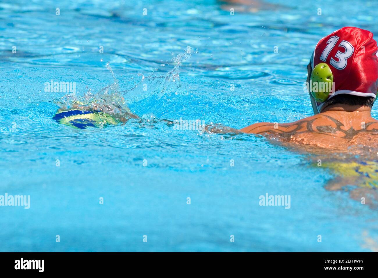 Rear view of a mid adult man playing water polo in a swimming pool ...