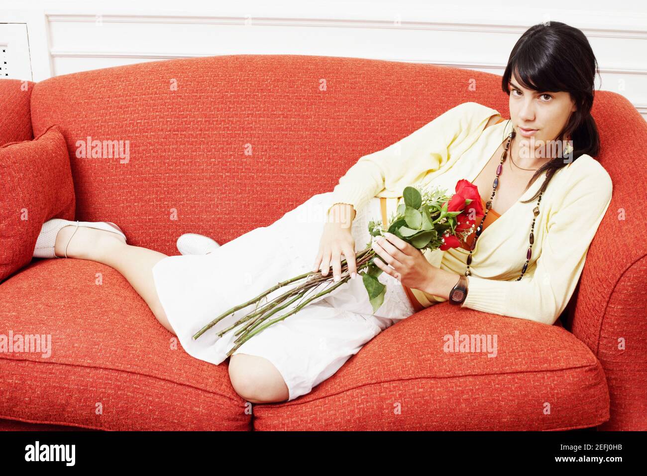 Portrait of a young woman reclining on a couch and holding a bunch of ...