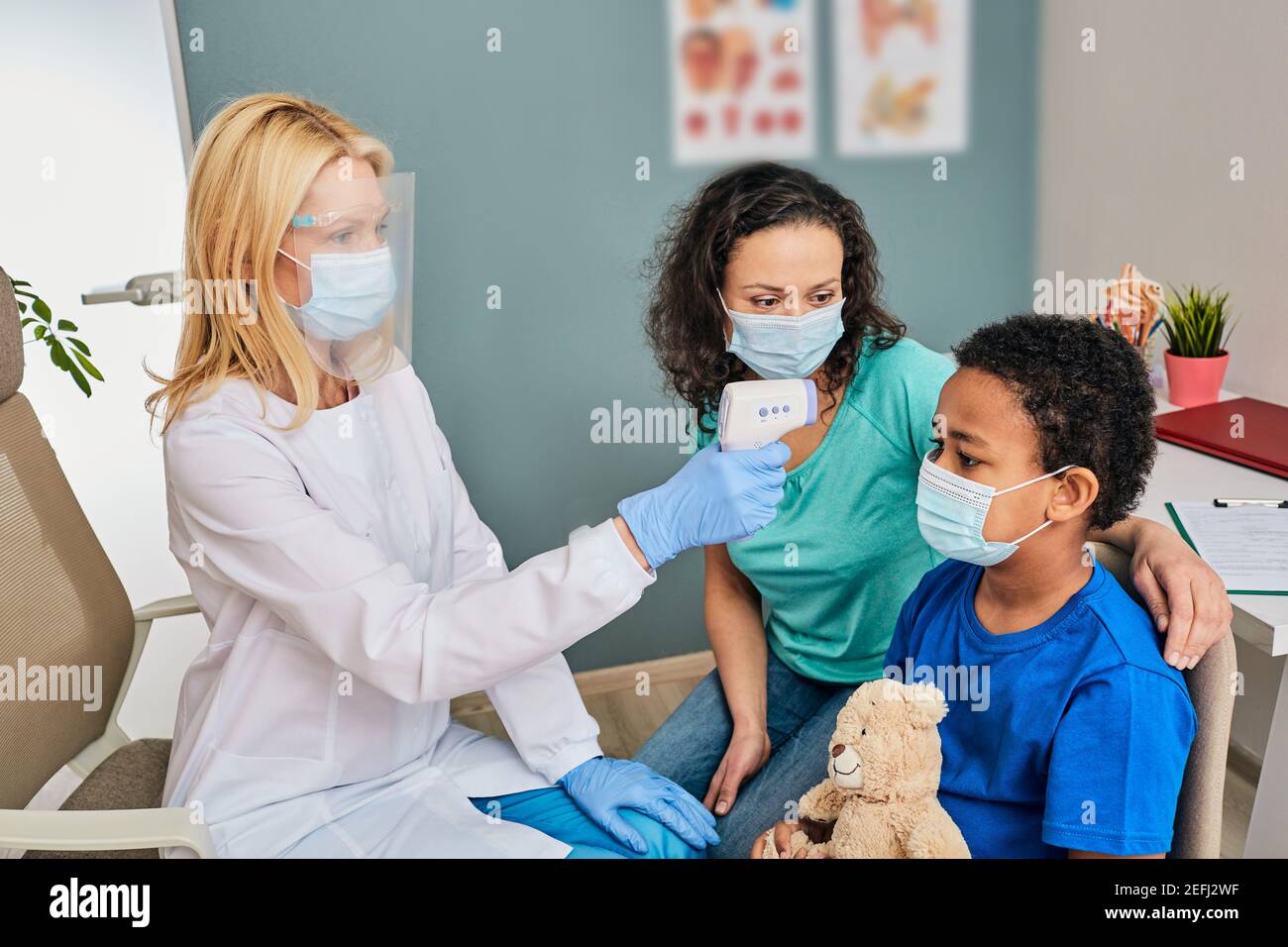 General practitioner using infrared thermometer measures boy body ...