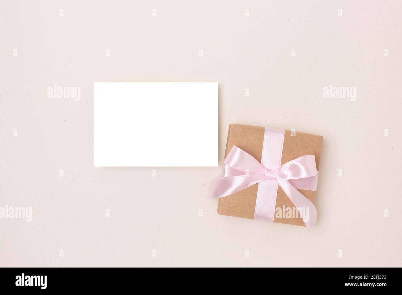 Empty paper sheet mockup and present tied with a pink ribbon on a beige ...