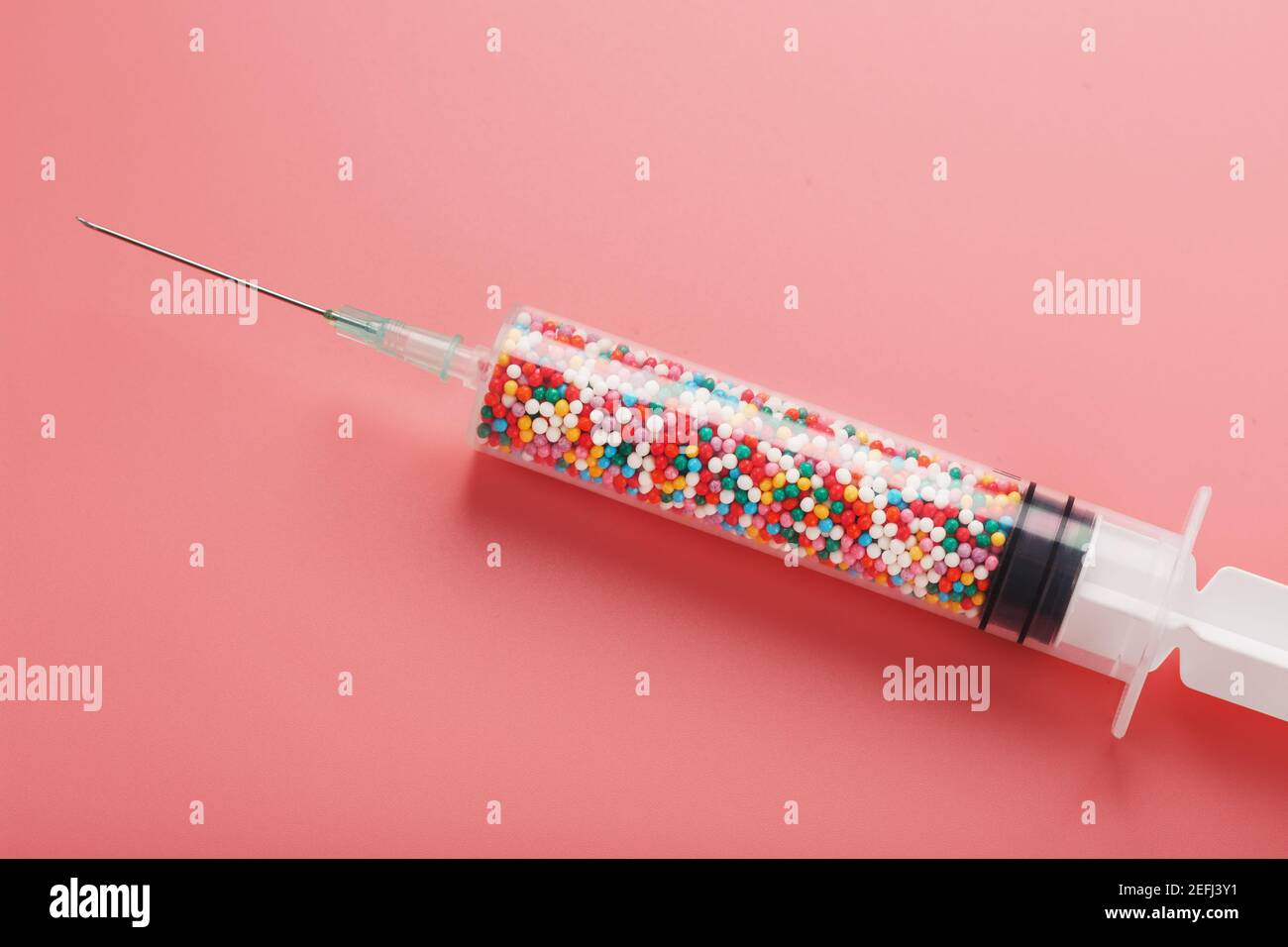 Medical Syringe filled with colorful balloons on a pink background with ...