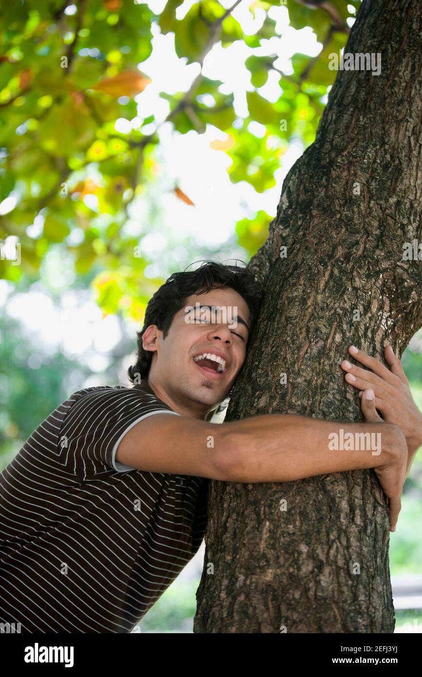 Young man hugging a tree trunk and laughing Stock Photo - Alamy