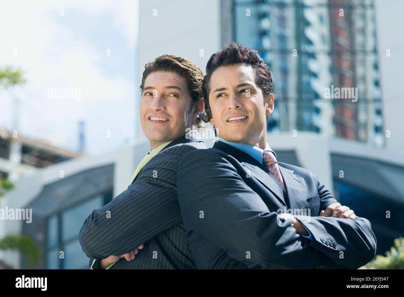 Two businessmen standing back to back and smiling Stock Photo - Alamy