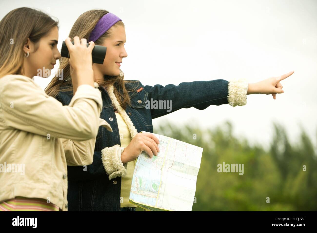 Teenage girl pointing forward with a girl looking through a pair of ...