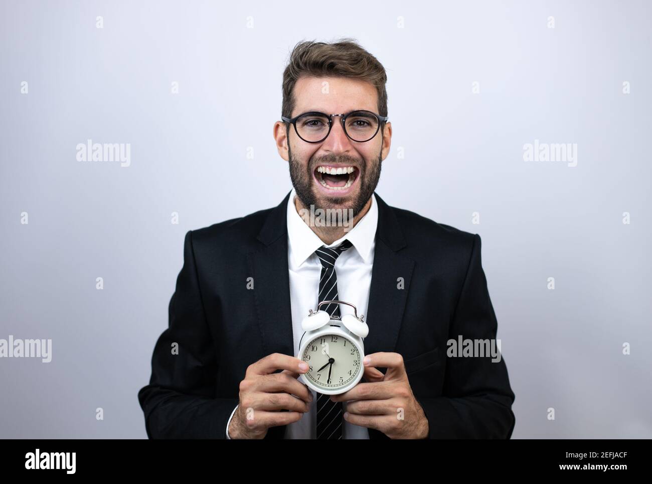 Young business man wearing suit screaming and scared, holding a clock ...
