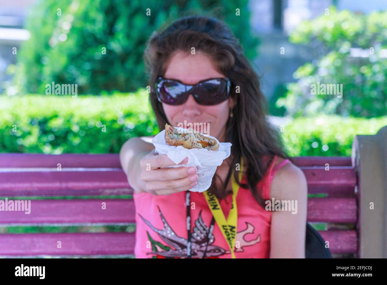 Young student woman offering a bite from her sandwich on a park bench ...