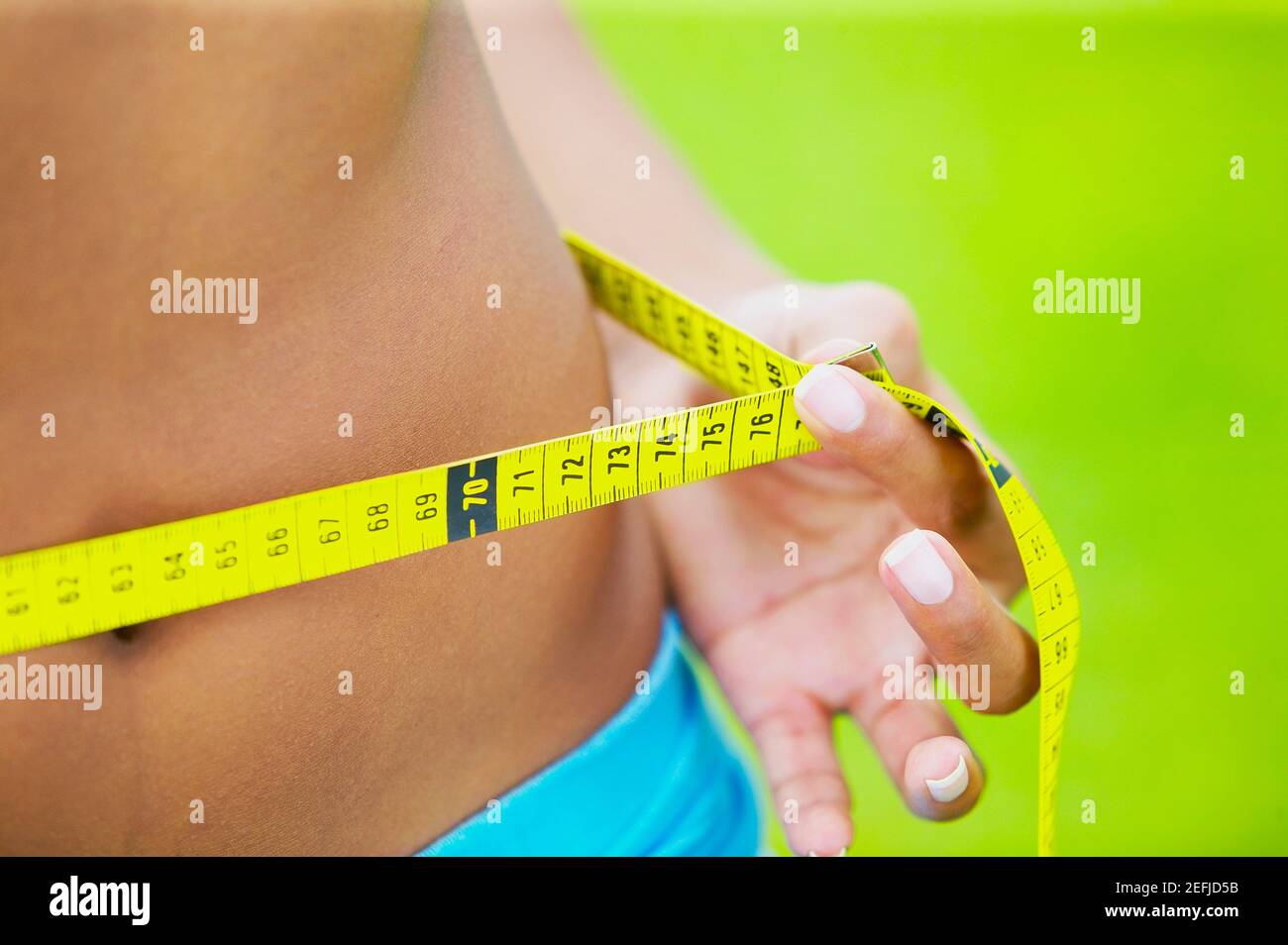 Mid section view of a woman measuring her waist with a tape measure ...