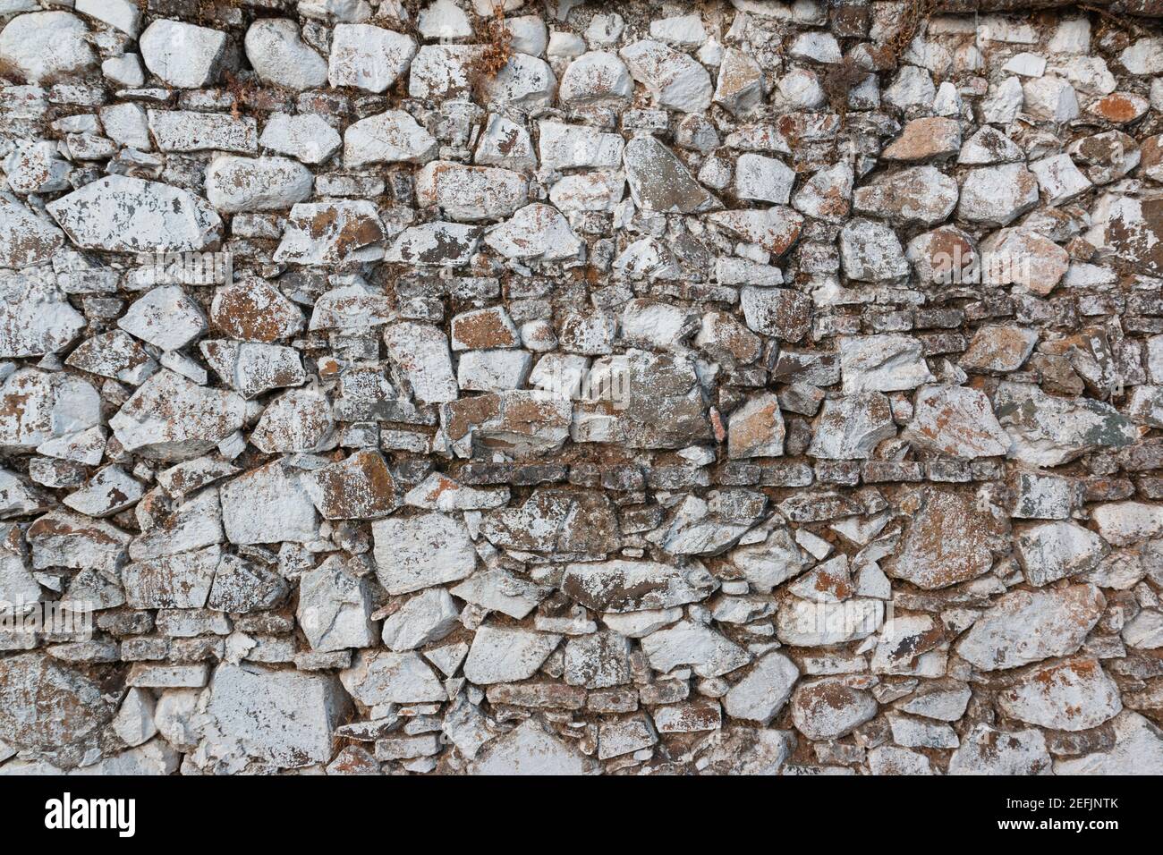 Old stone wall, painted in a faded white color and built with stones ...