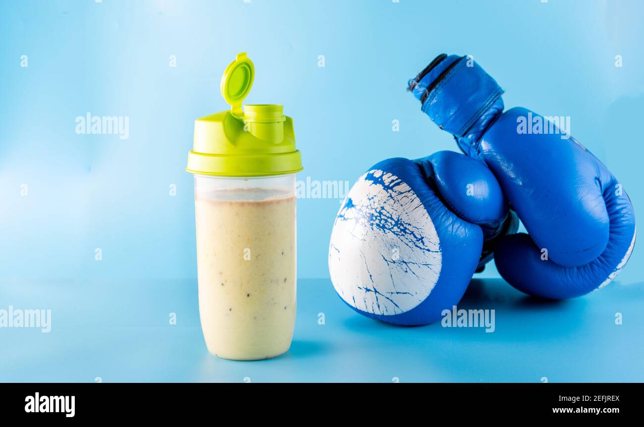 Shaker with cocktail and boxing gloves. Blue boxing gloves on a blue ...