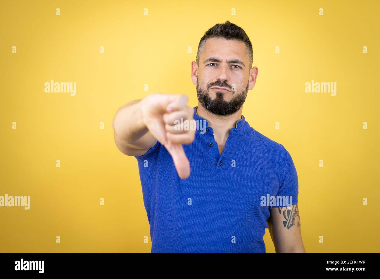 Handsome man with beard wearing blue polo shirt over yellow background ...