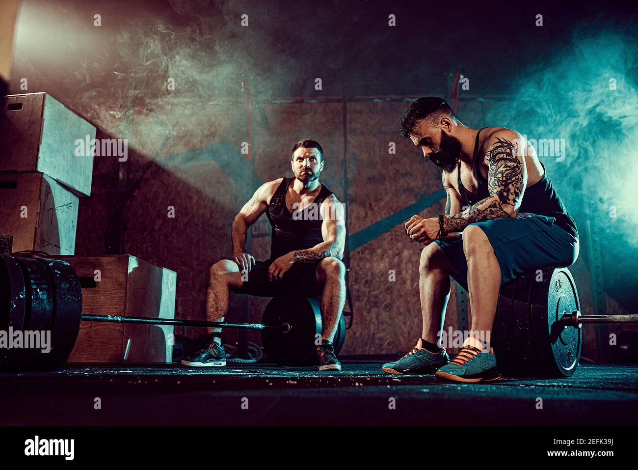 Two muscular bearded tattoed athletes relax after training, lifting ...