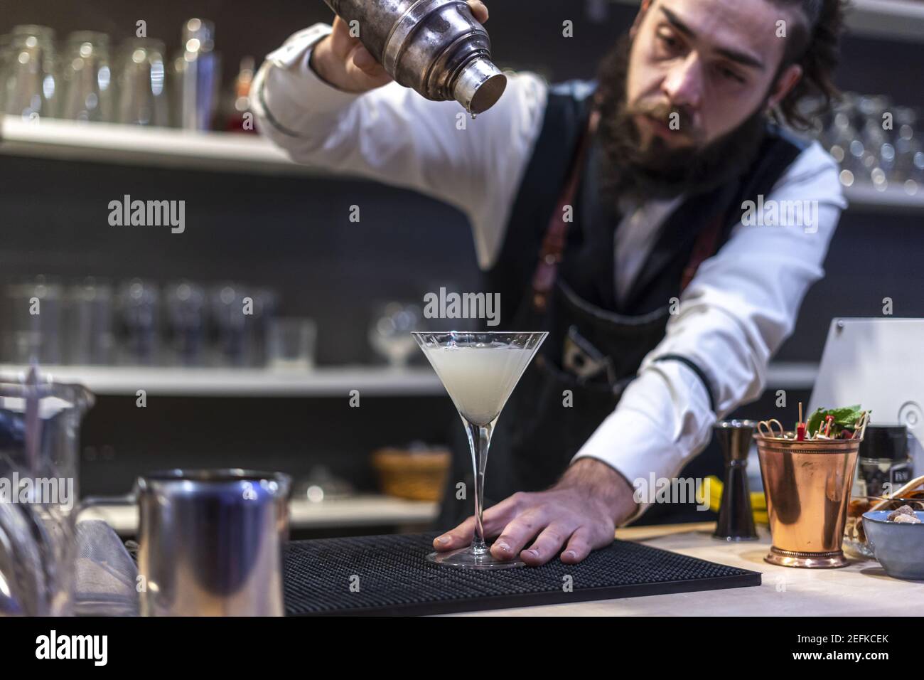 Bartender pouring a fresh alcoholic drink into the glasses with ice cubes on the bar counter ...