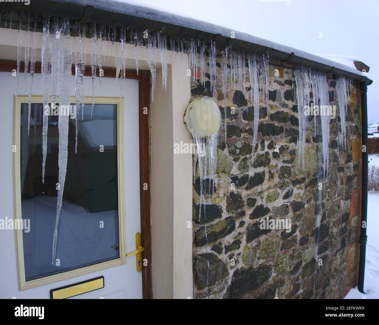 Large icicles hanging from the gutter and outdoor light of a stone ...