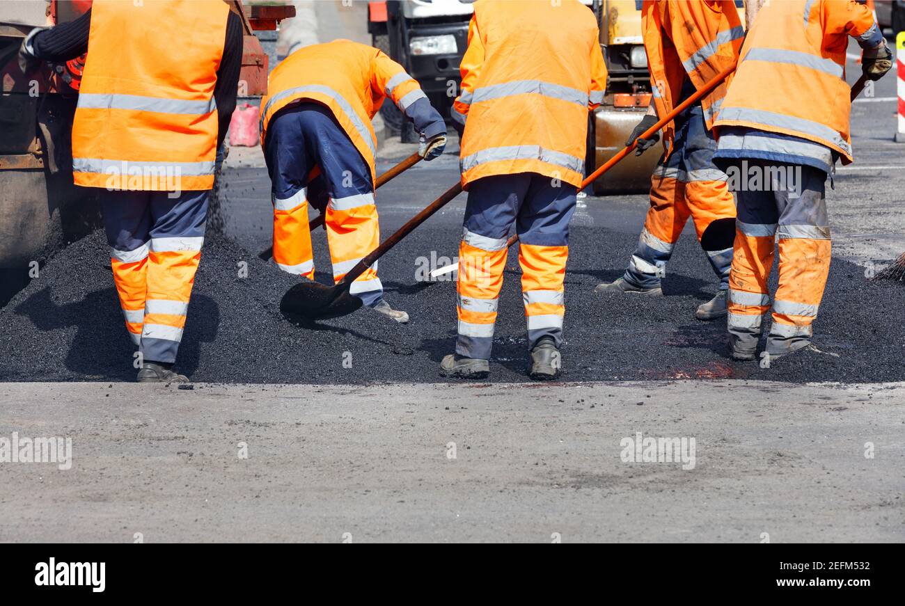 A team of road workers in orange reflective uniforms repair a section ...