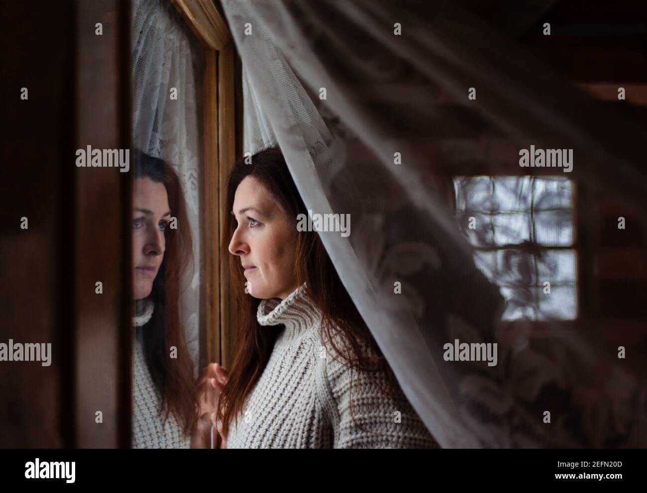 Attractive woman looking through window behind a lace curatin Stock ...
