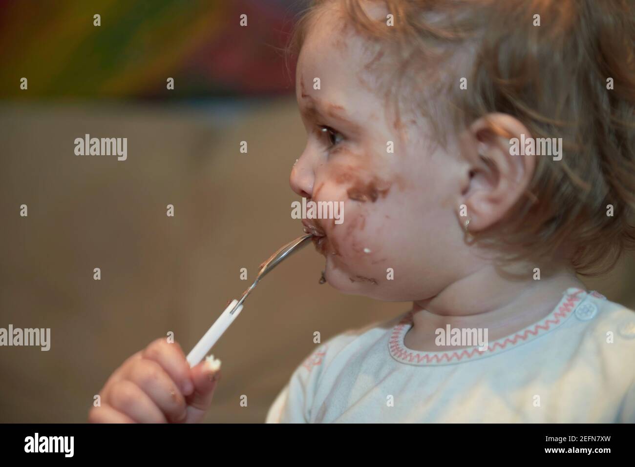 baby girl eating her chocolate desert with a spoon and making a mess ...