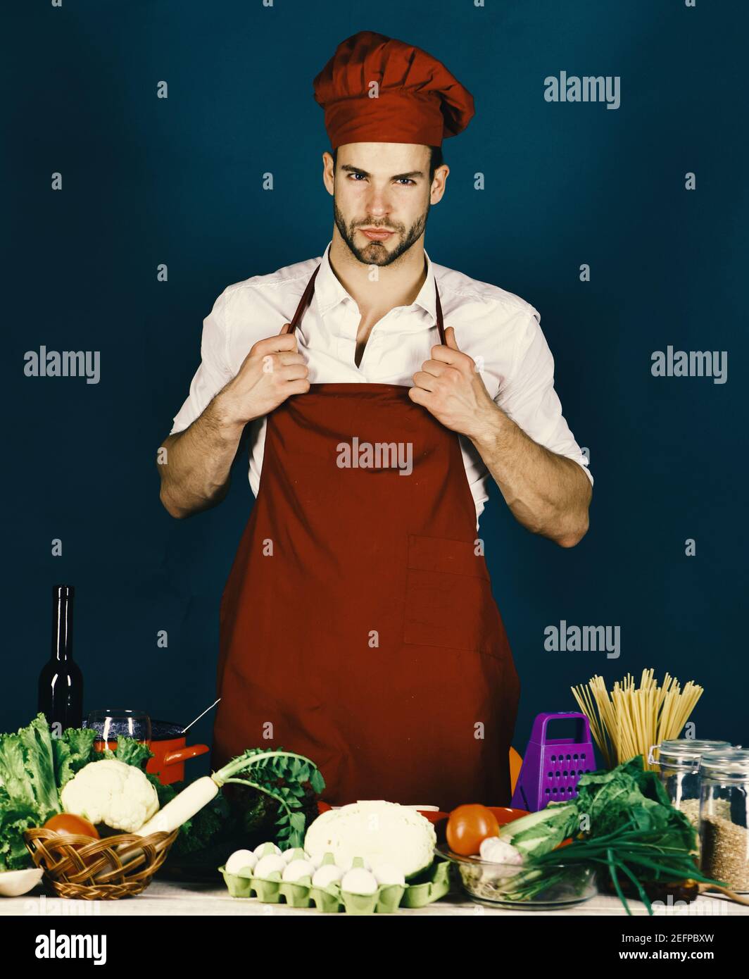 Cook works in kitchen near table with vegetables and tools. Man in cook ...
