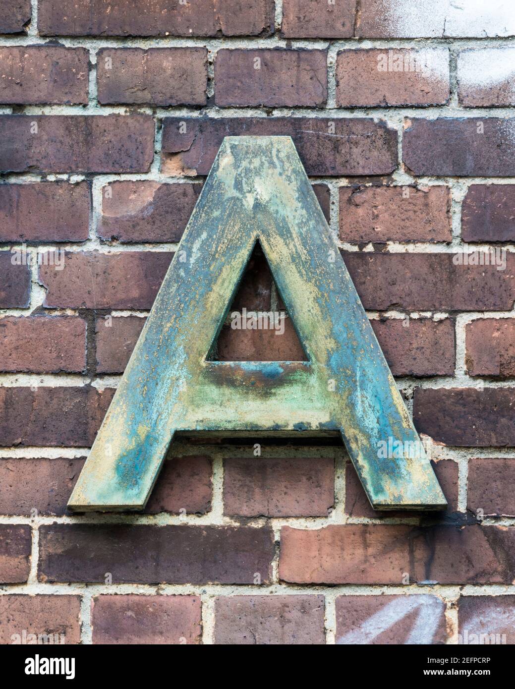 Green metal letter A in front of a brick wall Stock Photo - Alamy
