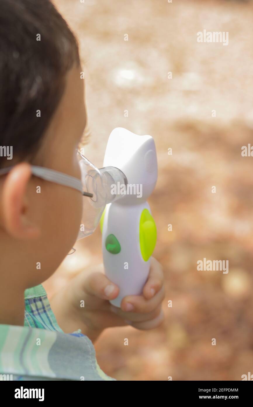 vertical closeup shot of a male child using a portable inhaler ...