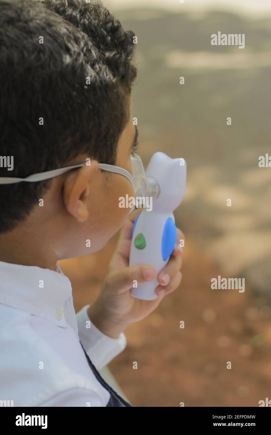 Vertical closeup shot of a male child using a portable inhaler ...