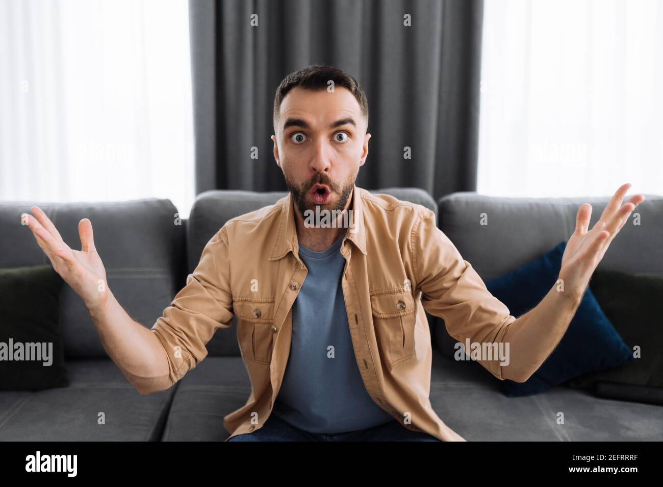 Shocked emotional man. Surprised caucasian guy sits on the couch ...