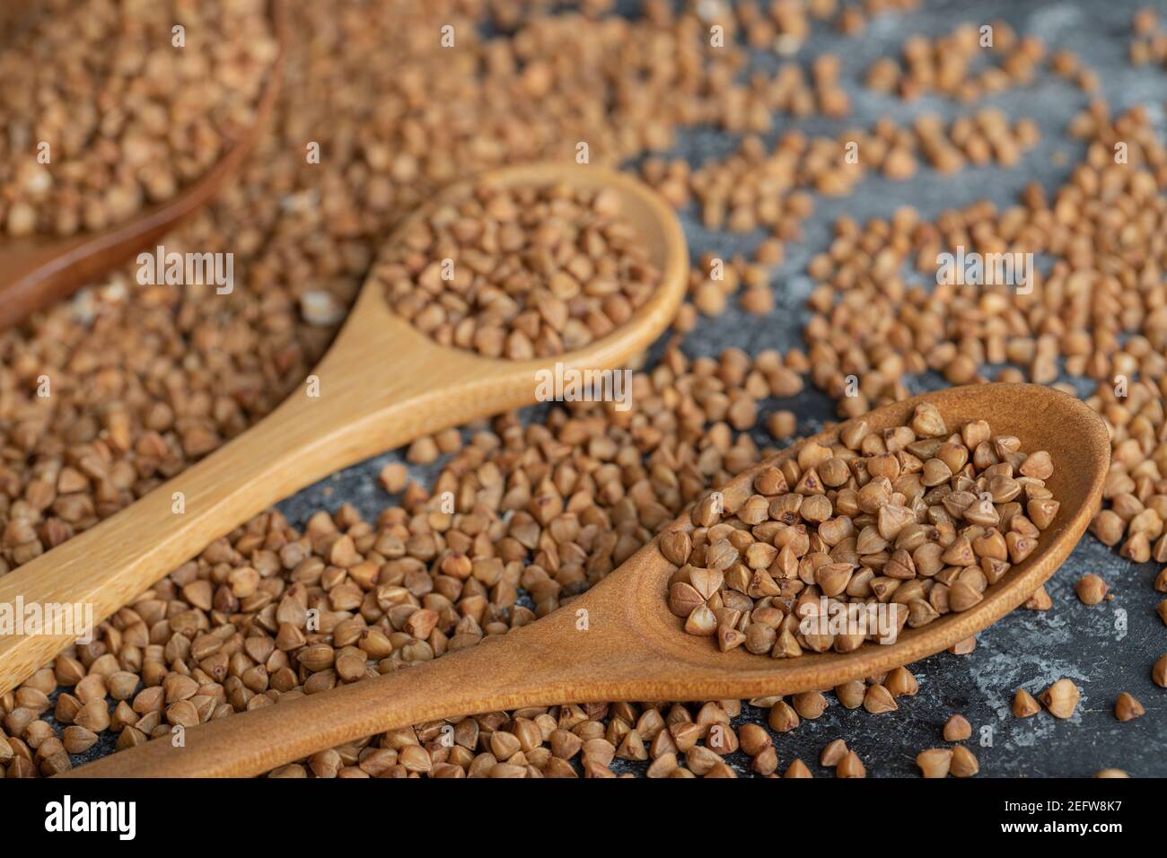 Two wooden spoons full of raw buckwheat Stock Photo - Alamy