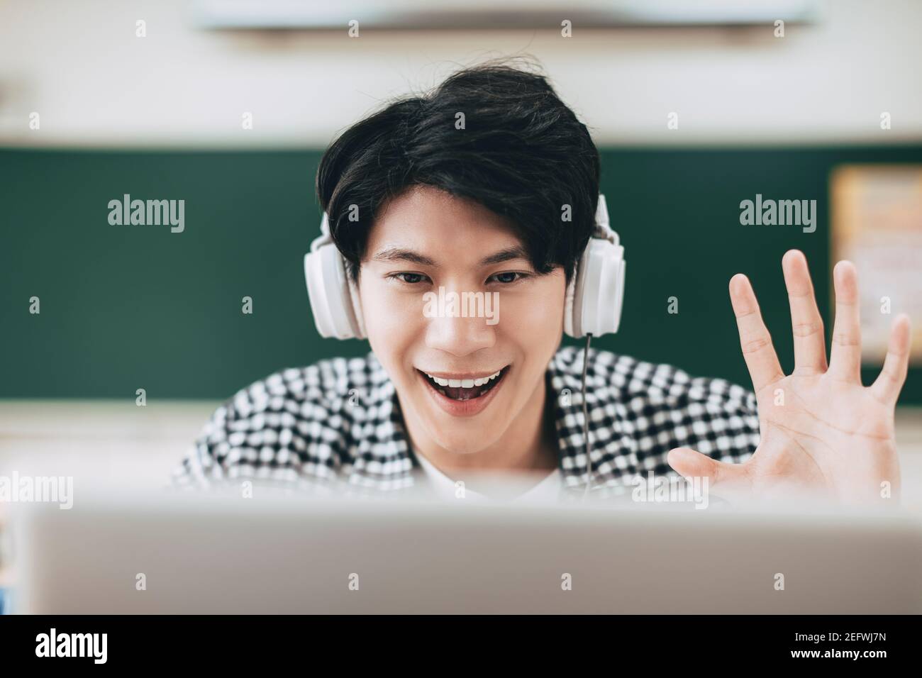 Young cheerful asian student using video call on laptop in classroom ...