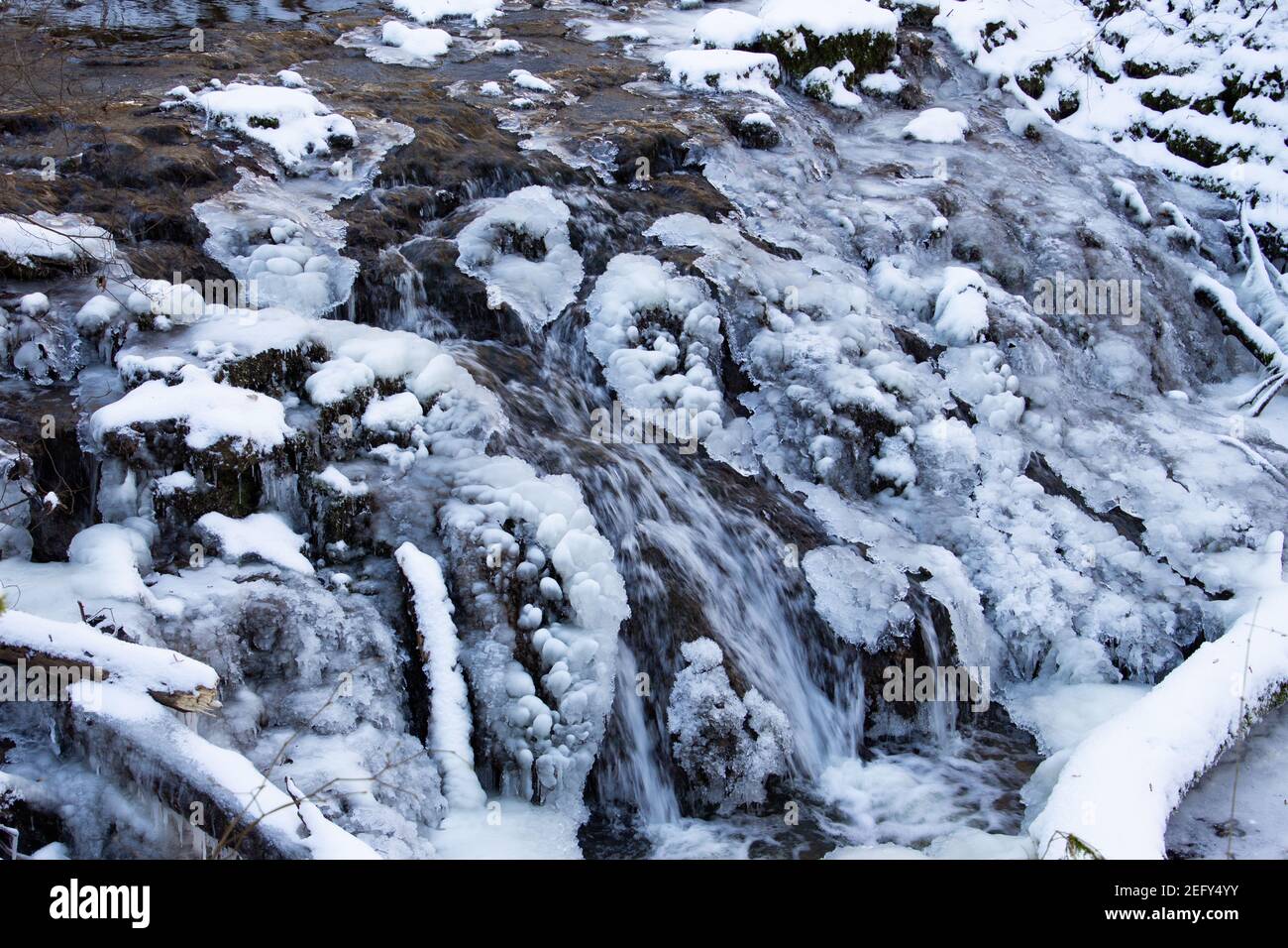 Small waterfall in a forest creek with frozen rocks and icicles Stock ...