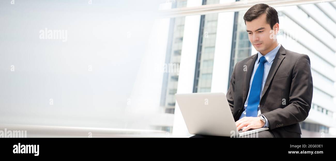 Businessman using laptop computer while sitting outdoor in the city ...