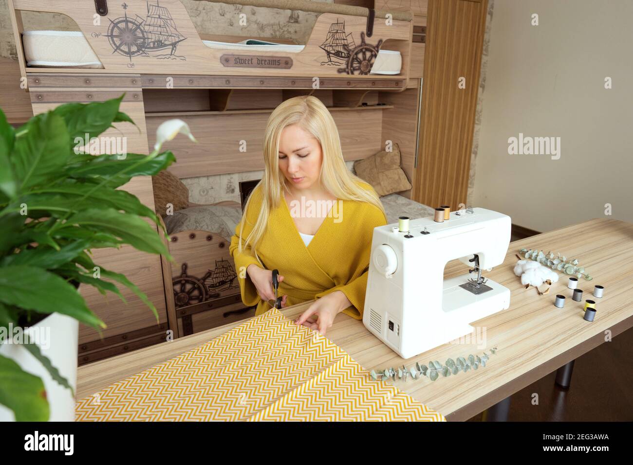 A woman sits at the sewing maching cutting a piece of cotton with the ...