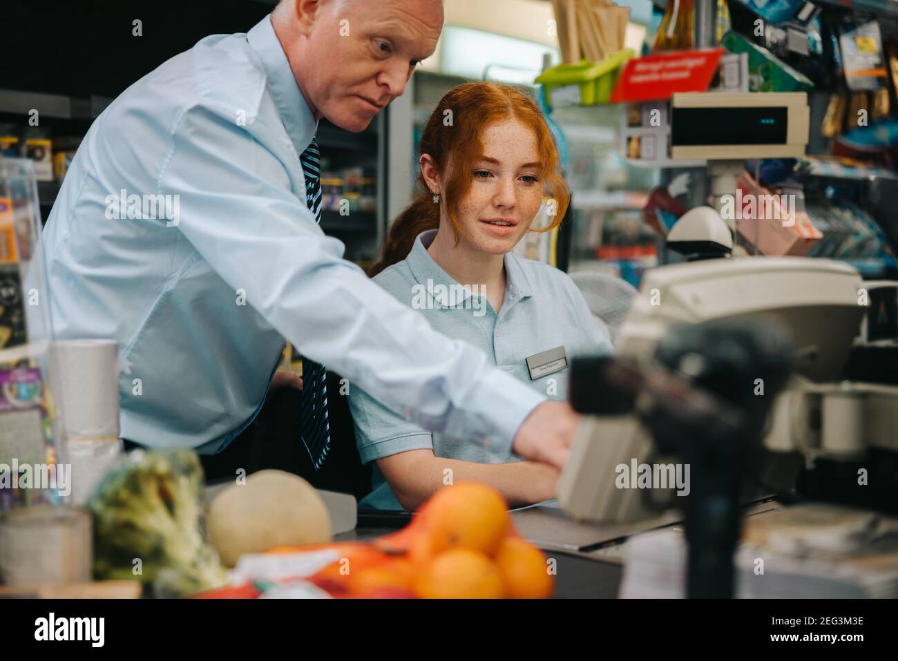 Senior manager showing the checkout process to new female employee in ...