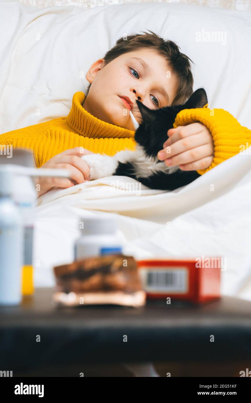 Sick child boy with digital thermometer in mouth lying in bed with ...