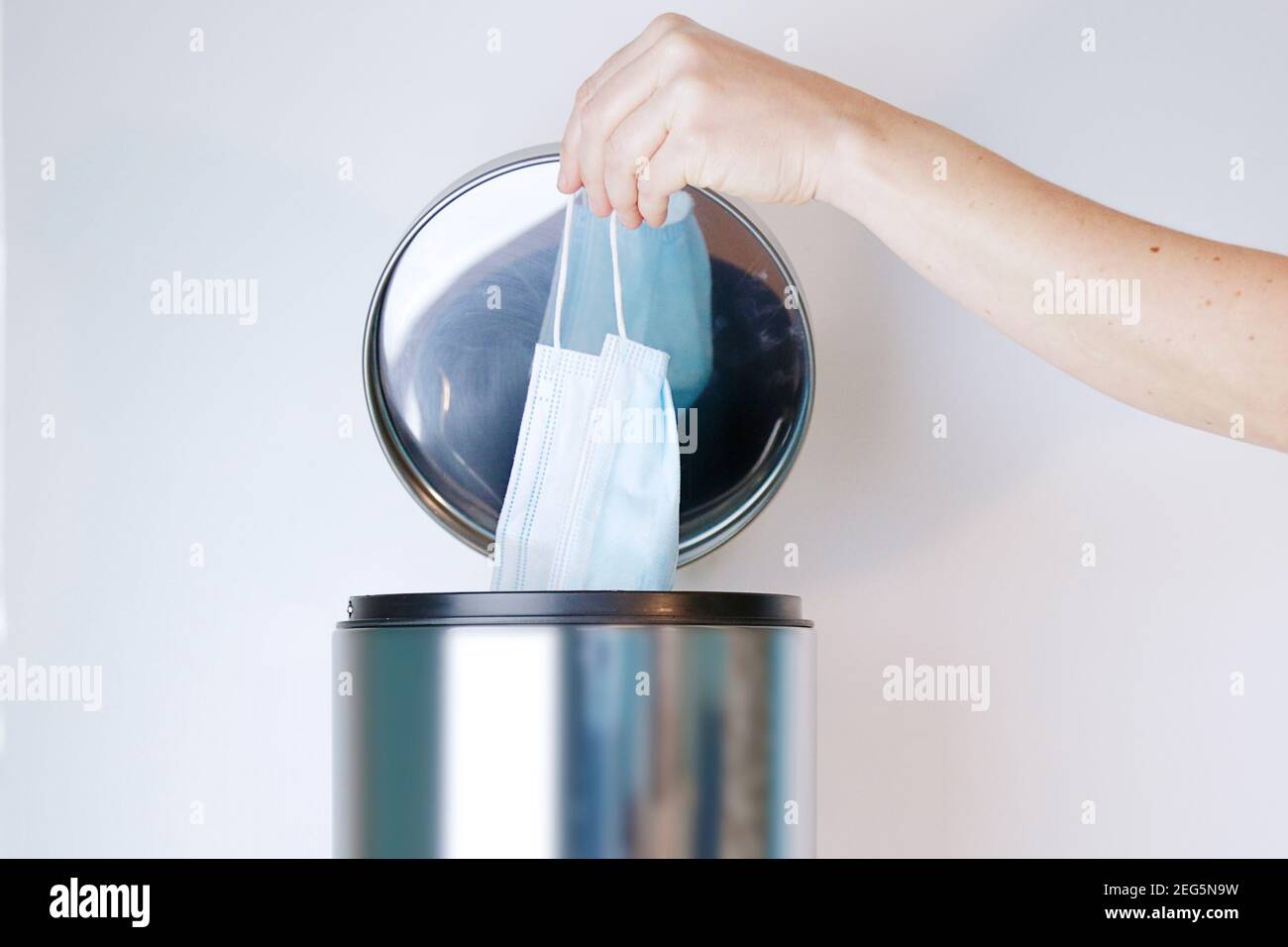 Woman hand throwing face mask into the garbage bin against background ...