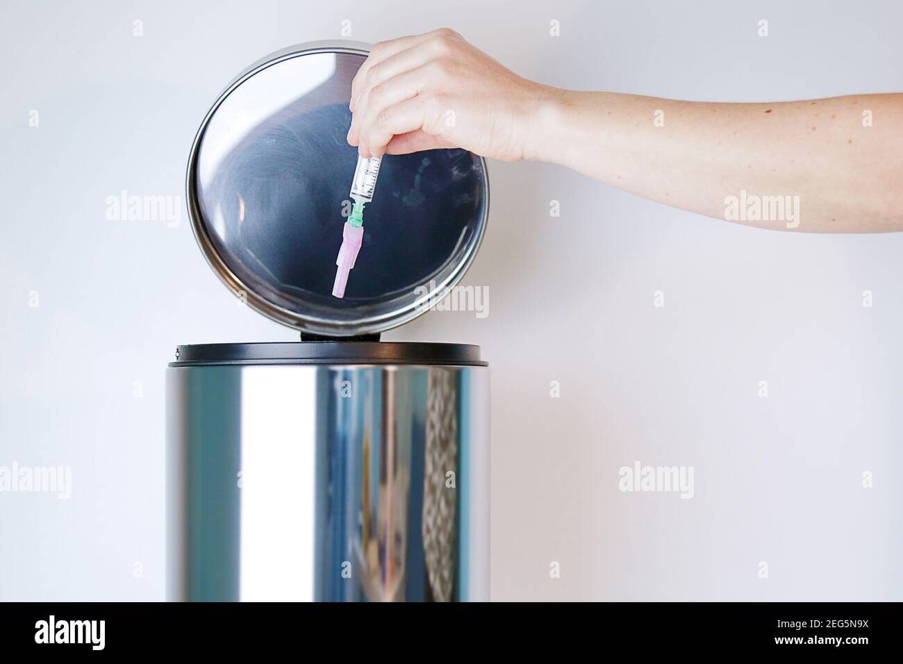 Woman hand throwing a syringe into the garbage bin against white ...