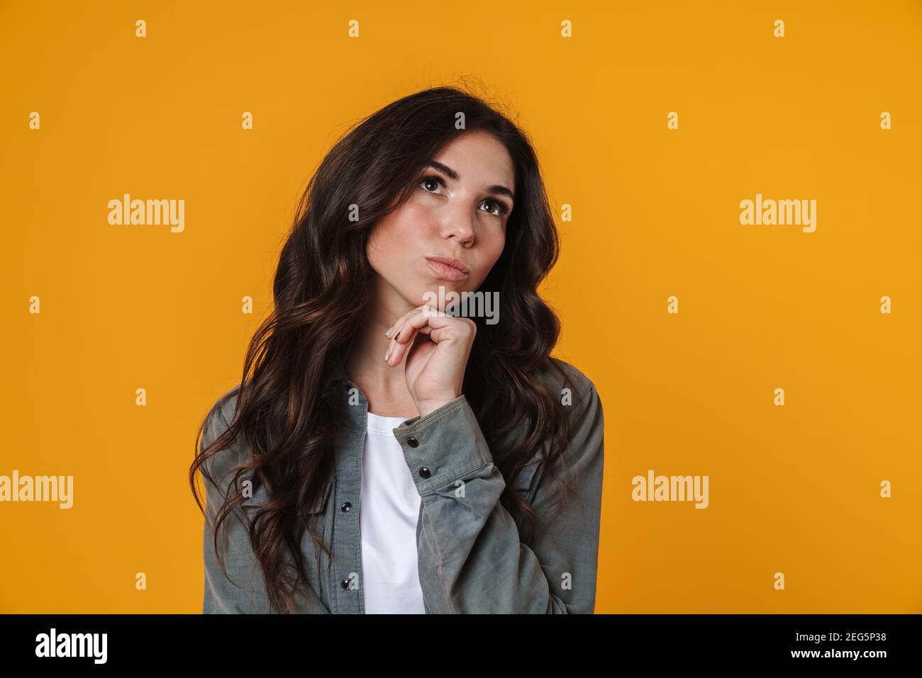 Thinking beautiful girl posing and looking upward isolated over yellow ...
