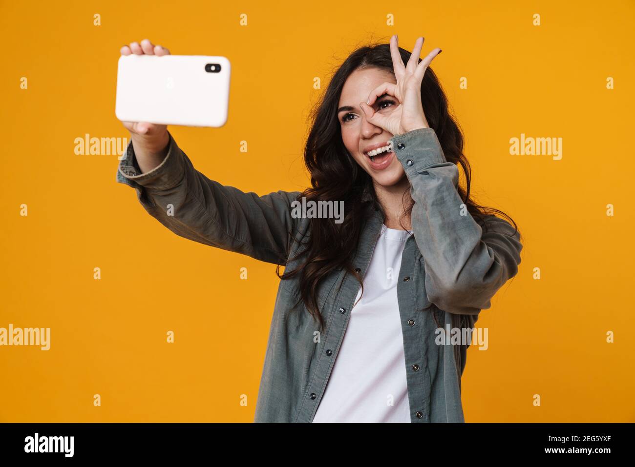 Happy beautiful girl showing ok sign while taking selfie on cellphone ...