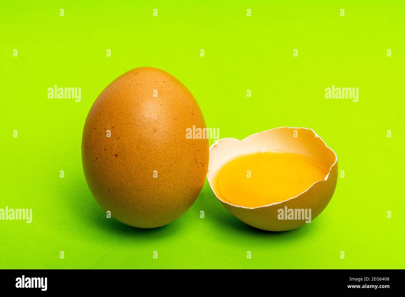 Brown egg and cracked shell with yolk on bright green background ...