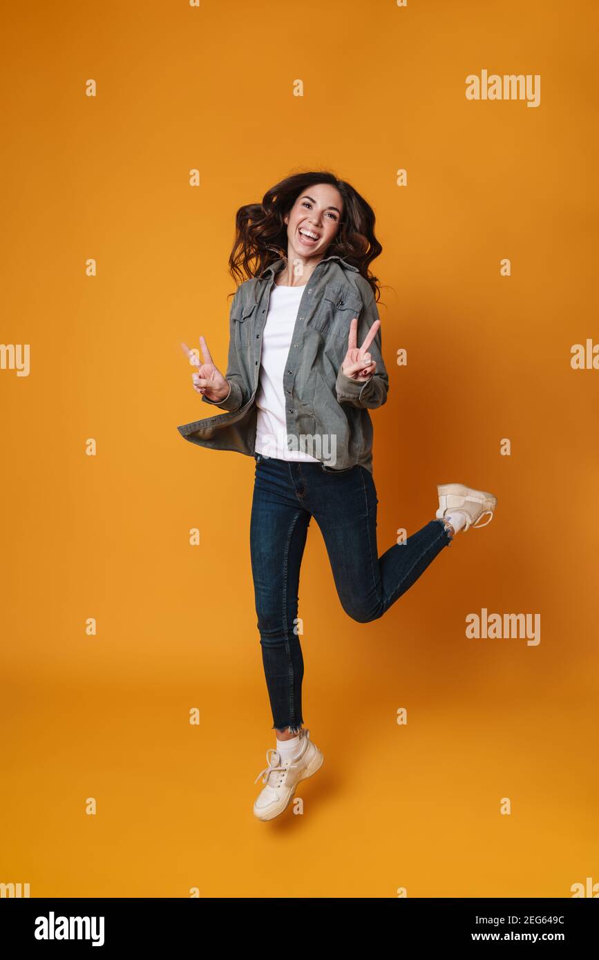 Excited beautiful girl showing peace sign while jumping isolated over ...