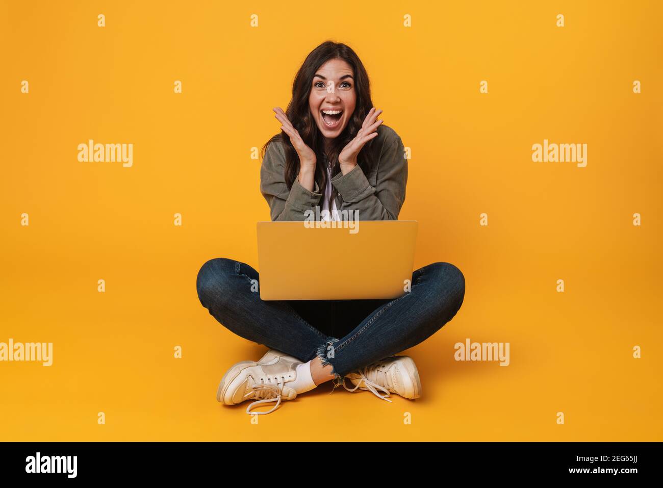 Excited girl screaming and using laptop while sitting on floor isolated ...