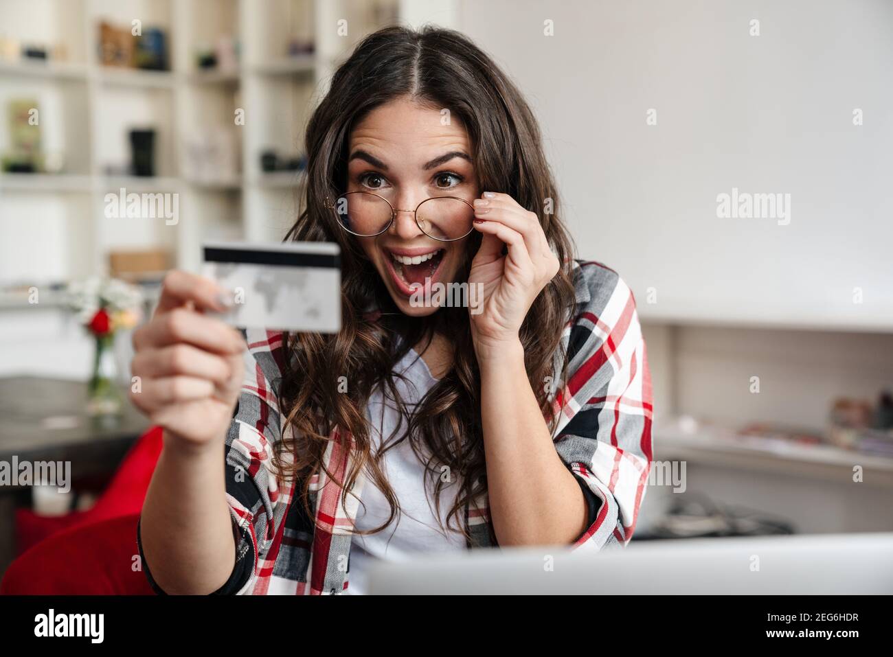 Excited brunette woman screaming and holding credit card while working ...