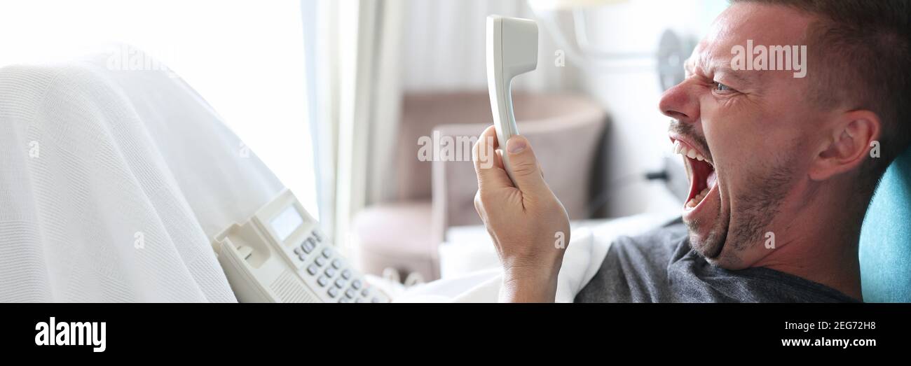 Angry man lies in bed and shout into white phone receiver Stock Photo ...