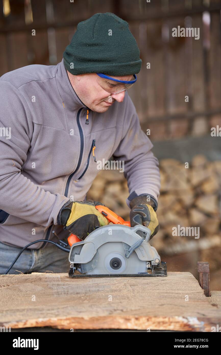 Carpenter using a hand circular saw with laser to cut a walnut board ...