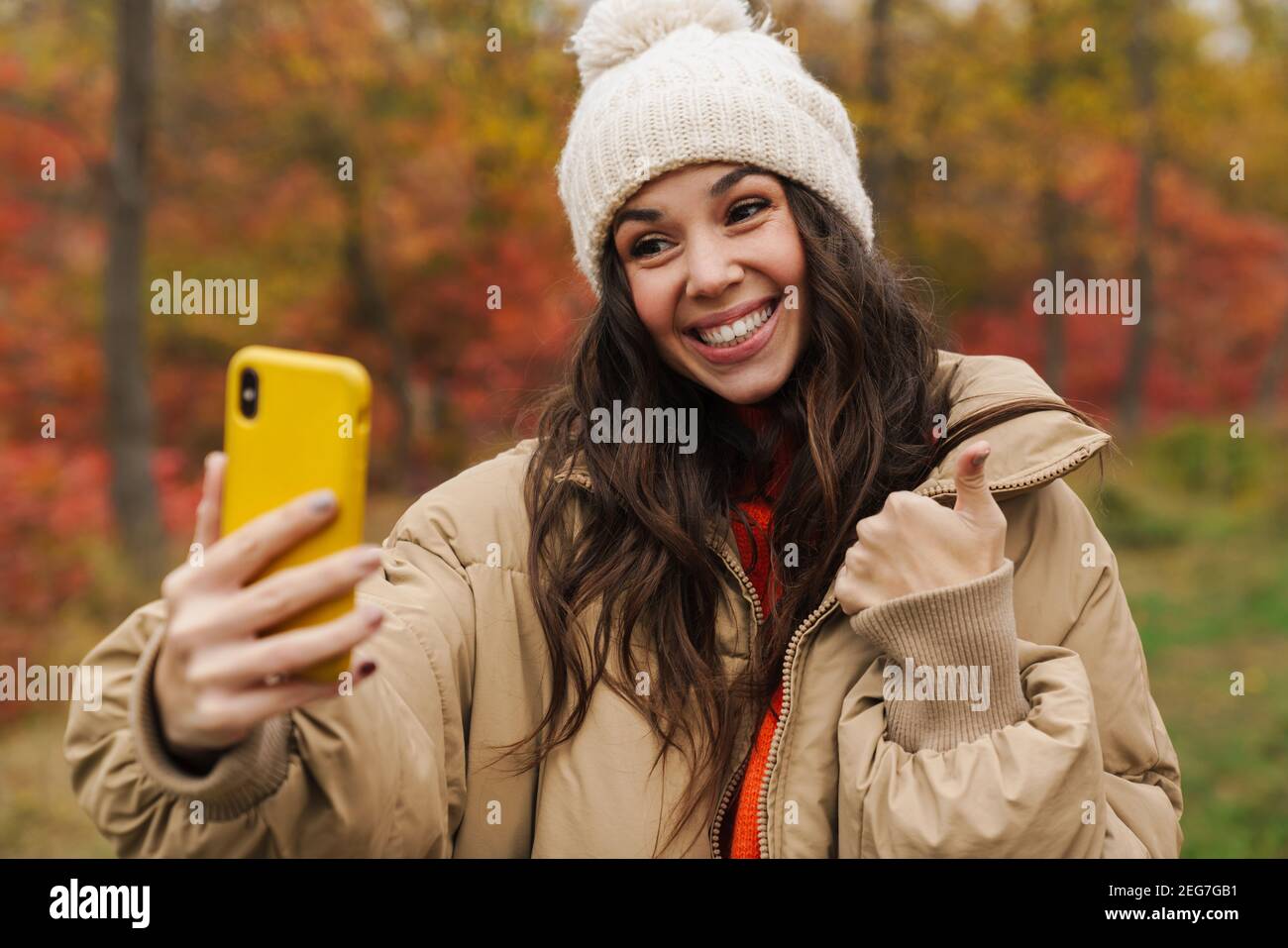 Brunette happy woman in knit hat taking selfie on cellphone while ...