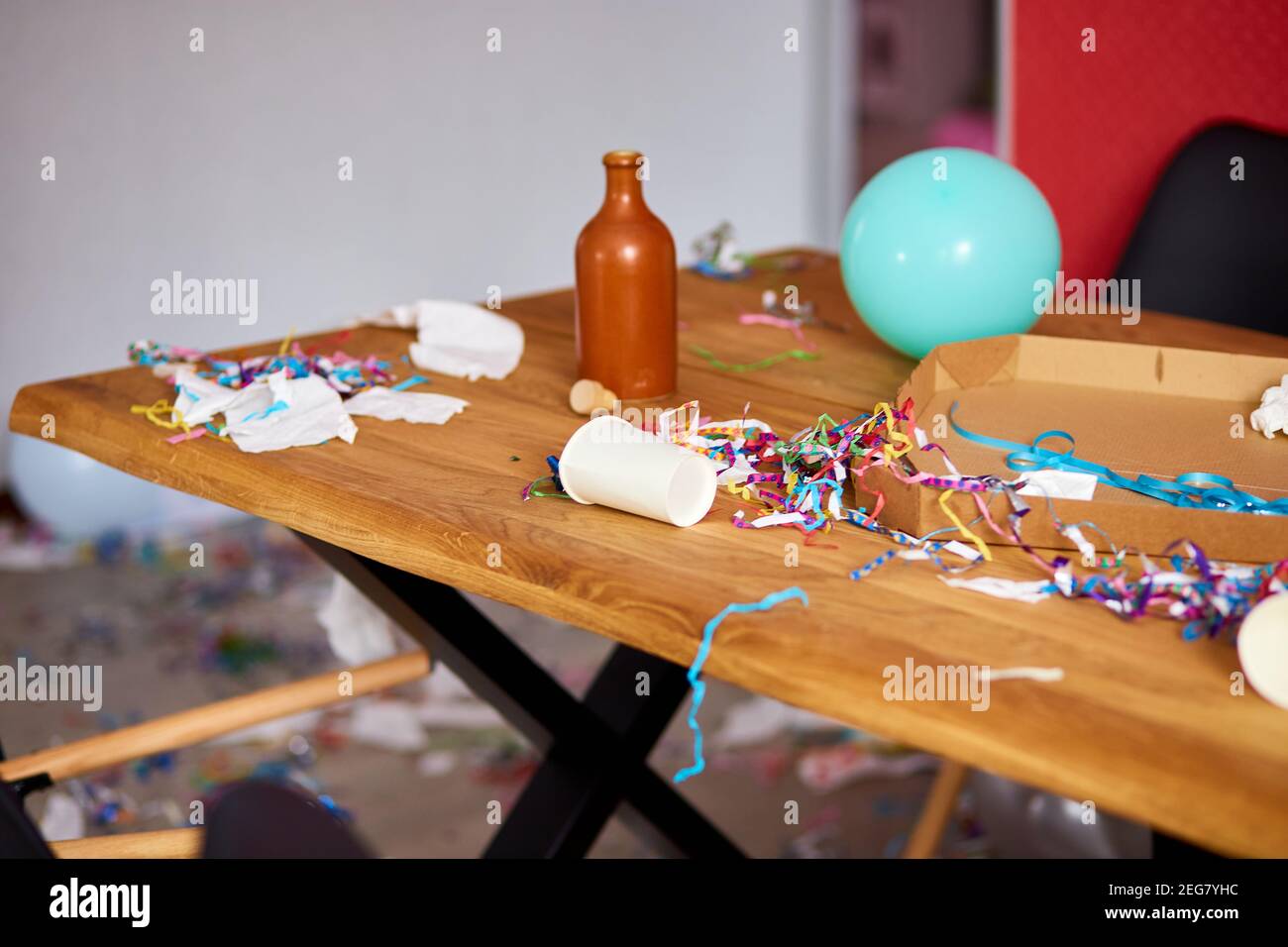 Messy wooden table with pizza box, empty blue bottles, wine glass and ...