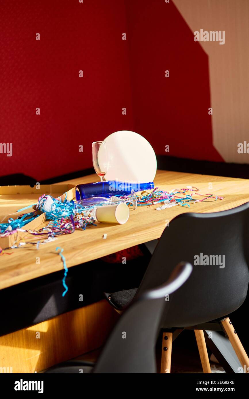 Messy wooden table with pizza box, empty blue bottles, wine glass and ...